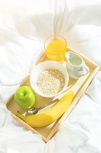하얀 담요 침대 시트에 건강 한 아침 식사 재료로 나무 쟁반 투 수 오렌지 주스 바나나에 너트 우유를 그릇에 귀리 그린 애플 밝은 아침 햇빛 창문을 통해 스트리밍입니다 공간