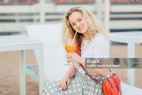 친절한 미소 건강한 순수한 피부를 가진 즐거운 여성 모델 칵테일 잔을 들고 세련된 옷을 입고 여름 방학 동안 해변에서 Recreats 좋은 분위기입니다 사람과 라이프 스타일