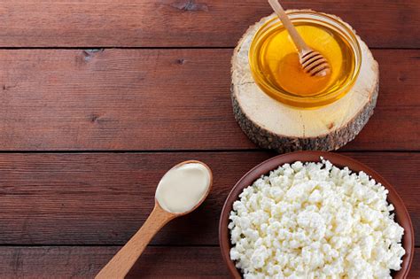 코 티 지 치즈와 크림입니다 부드러운 치즈와 꿀 나무 보드에 도자기에 코 티 지 치즈입니다 나무로 되는 숟가락에 크림입니다 나무 스탠드에 여 보 공간 복사 갈색에 대한 스톡