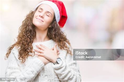 젊은 갈색 머리 소녀 얼굴에 닫힌된 눈으로 가슴에 손을 감사와 함께 웃 고 고립 된 배경 위에 크리스마스 모자를 쓰고 건강 개념입니다 감사에 대한 스톡 사진 및 기타 이미지