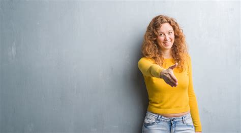 웃 고 인사 하 고 환영으로 제공 하는 친절 한 악수 회색 그런 지 벽에 빨강 머리 젊은 여자 성공적인 사업입니다 곱슬 머리에 대한 스톡 사진 및 기타 이미지 Istock