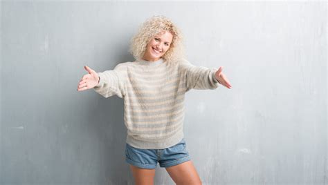 포옹에 대 한 두 팔을 벌려 웃 고는 카메라를 보고 그런 지 회색 배경 위에 곱슬 머리를 가진 젊은 금발 여자 명랑 식 수용 행복입니다 곱슬 머리에 대한 스톡 사진 및 기타