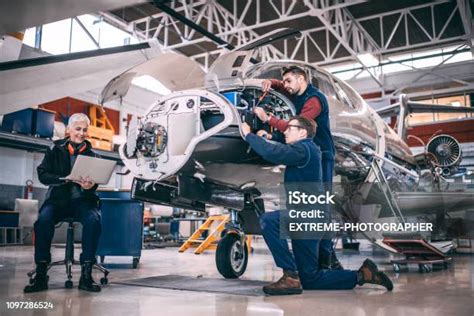노인 여성 항공기 엔지니어 앉아서 격납고에서 작은 비행기에 일 손 도구를 사용 하는 그녀의 동료를 돕는 그녀의 노트북을 사용 하 여 항공우주 산업에 대한 스톡 사진 및 기타