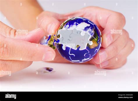 Hands Inserting A Puzzle Piece Into A Globe With Sections Missing Representing Global Unity And