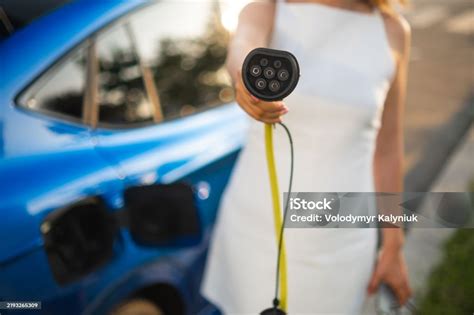 클로즈업 한 여자는 배경에 파란색 자동차와 함께 손에 전기 자동차 충전기를 들고 있습니다 30 34세에 대한 스톡 사진 및 기타 이미지 30 34세 교통수단 네트워크