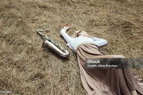 색소폰 옆에 마른 잔디에 누워 긴 드레스에 아름다운 젊은 여성의 몸 건초에 여름에 소녀는 악기 자연에 휴식의 개념과 함께 휴식 Theatrical Performance에