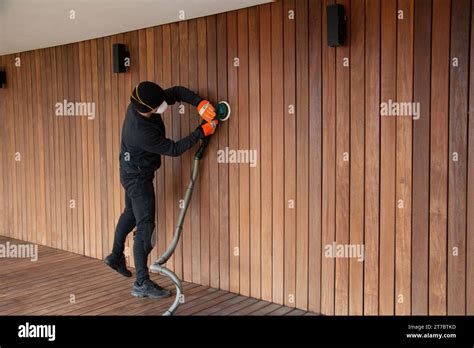 Deck Worker In Mask Sanding Hardwood Siding With Orbital Sander Wooden Deck And Cladding Deck Worker In Mask Sanding Hardwood Siding With Orbital Sander Wooden Deck And Cladding