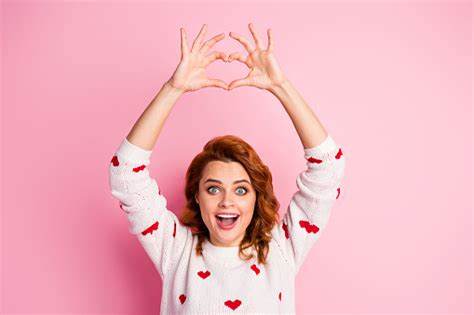 그녀의 클로즈업 초상화 그녀의 좋은 매력적인 사랑스러운 기쁜 쾌활한 쾌활한 쾌활한 물결 모양의 머리 소녀 를 입고 흰색 풀오버 를 보여주는 하트 가입 Amour 날짜 핑크