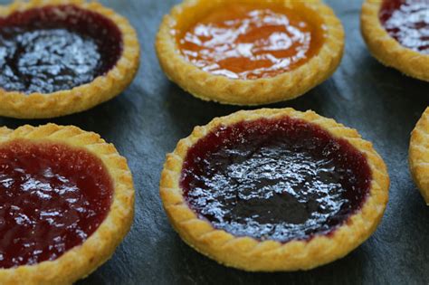 딸기 라즈베리 살구 잼으로 채워진 쇼트 크러스트 페이스트리가 있는 작은 수제 잼 타르트 파이의 이미지 애프터눈 티 어린이 생일 파티 음식 뷔페 플래터용 검은 나무 배경이