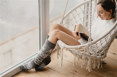 니트 스웨터와 따뜻한 양말을 입은 여성 창 가까스로 스윙에 여유와 독서 책 양말에 대한 스톡 사진 및 기타 이미지 양말 읽기 그네 Istock
