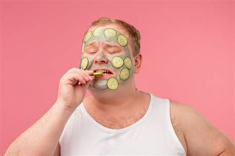 얼굴에 오이 마스크를 가진 뚱뚱한 남자 분홍색에 고립 된 오이 조각을 먹는다 건강에 좋지 않은 음식에 대한 스톡 사진 및 기타