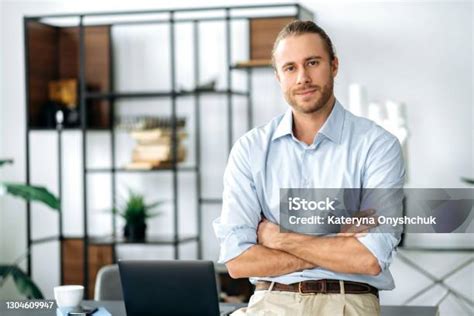 잘 생긴 자신감 매력적인 백인 세련된 옷을 입은 사람 디자이너 프리랜서 또는 직원 그의 책상 근처에 서 팔을 교차 카메라를보고