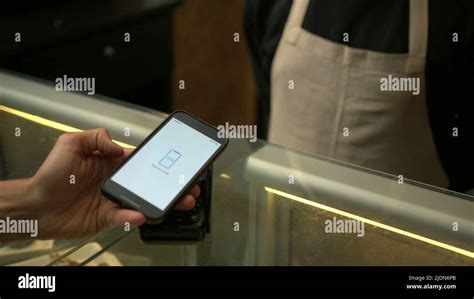 Customer Paying With Contactless NFC Payment Technology On Smartphone Device Inside Business