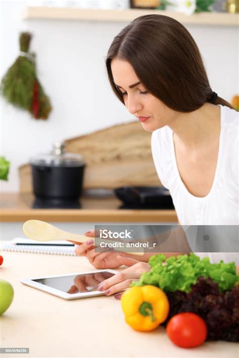 아름 다운 스페인 여자는 부엌에서 태블릿 컴퓨터를 사용 하는 동안 요리 저녁 이나 아침 식사에 대 한 새로운 레시피를 발견 하는