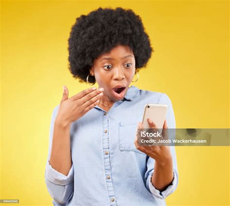 노란색 배경에 고립된 스튜디오에 있는 흑인 여성의 전화 놀라움과 충격 와우 핸드폰과 소셜 미디어 Omg 또는 Wtf 이모티콘에서 가짜 뉴스를 읽기 위해 스마트폰으로 놀란