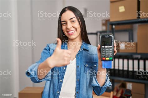 신용 카드와 데이터 폰을 들고 중소기업 전자 상거래에서 일하는 히스패닉 여성은 행복하고 긍정적 인 미소를 지으며 엄지 손가락을 치켜 들고 우수하고 승인 기호를 수행합니다