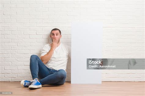 손으로 물 커버 입의 흰색 벽돌 벽 잡고 병 앉아 젊은 백인 남자는 실수 두려움 침묵 비밀 개념에에서 무서 워의 표현에 대 한 수치와 충격 가리기에 대한 스톡 사진 및 기타