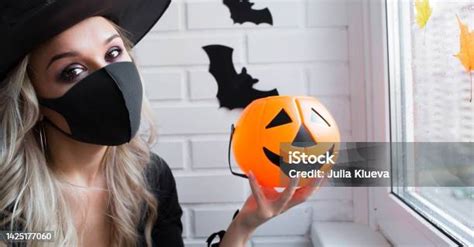 검은 마녀 의상을 입은 슬픈 금발과 얼굴 마스크가 창문 밖을 바라 봅니다 코비드로부터 할로윈 보호 준비 10월에 대한 스톡 사진 및 기타 이미지 Istock