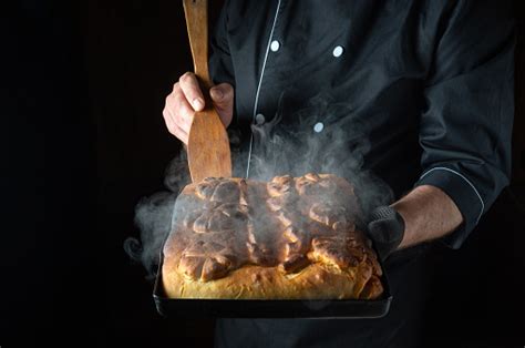 제빵사는 갓 구운 빵이 담긴 김이 모락모락 나는 쟁반을 들고 있고 빵의 황금빛 껍질은 부엌 조명의 부드러운 빛 아래에서 반짝입니다 향기가 공기를 가득 채우고 모든 사람을 그