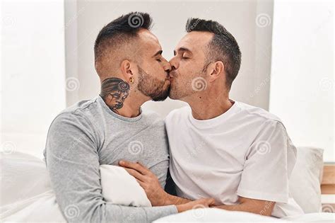 Two Men Couple Sitting On Bed Hugging Each Other Kissing At Bedroom