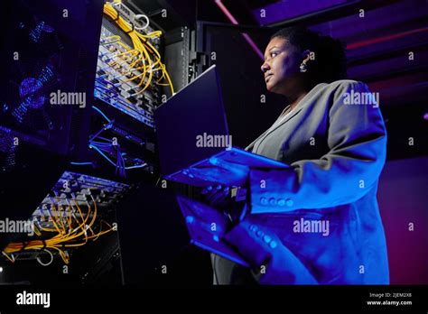 Low Angle Portrait Of Female Network Engineer Setting Up Servers In Data Center Lit By Neon