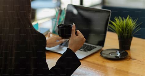 커피 컵을 들고 카페에서 나무 테이블에서 노트북으로 작업하는 사업가의 자른 샷 사진 Unsplash의 컵 이미지