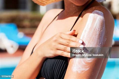 화창한 여름 날에 수영장 옆에서 무두질 한 어깨에 손으로 선 크림을 바르는 예쁜 여성 휴가 개념의 자외선 차단 요소 수영장