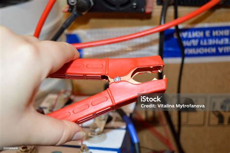손으로 들고 빨간 점퍼 케이블 클램프 배터리 시스템 연결된 배선 설정 전문 전기 환경 에너지 저장 자동차 수리 독립형 전력 솔루션 충전 유지 재생 가능 에너지 긴급출동