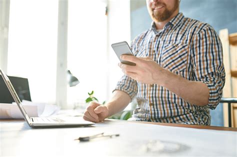 사무실에서 스마트 폰에 노트북 및 청사진 및 응답 Sms와 책상에 앉아 긍정적 인 젊은이의 클로즈업 건설 산업에 대한 스톡 사진 및 기타 이미지 Istock