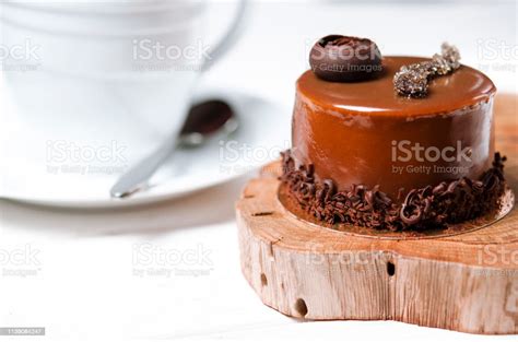 화이트 테이블에 흰색 컵 옆에 있는 나무 스탠드에 초콜릿 조각이 있는 맛 있는 초콜릿 케이크가 놓여 있습니다 그릇에 대한 스톡