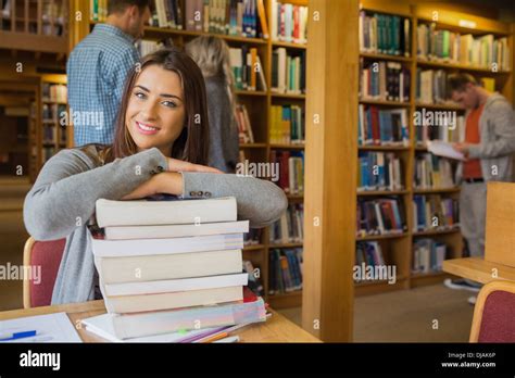 Female Student With Stack Of Books While Others In Background At