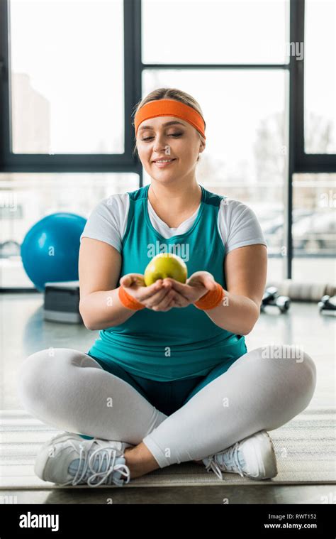 Happy Plus Size Woman Sitting On Fitness Mat With Crossed Legs And