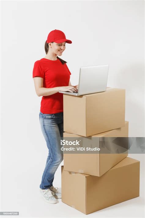 전체 길이 빨간 모자에 배달 젊은 여자의 초상화 T셔츠는 흰색 배경에 고립 여성 택배 노트북 Pc 컴퓨터와 빈 골 판지 상자 근처에 서 수신 패키지입니다 공간 복사 가냘픈에