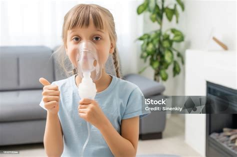 아이 소녀는 분무기로 흡입을합니다 흡입기를 손에 들고 집에서 흡입기를 통해 호흡하는 아픈 아이 건강관리와 의술에 대한 스톡 사진