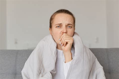 담요 아래에 두통이 있는 아픈 여성의 초상화 기침 입 가까이에 손을 잡고 슬픈 표정을 지으며 인플루엔자 증상을 보입니다 감기와 독감에 대한 스톡 사진 및 기타 이미지