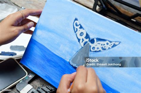 클로즈업 붓을 들고 있는 여성 견습 화가의 손 나무 천의 네 모서리에 고래와 바다를 칠하십시오 교사에게 보내기 전에 색상을 아름답게 장식하십시오 학교 미술 수업에서 20