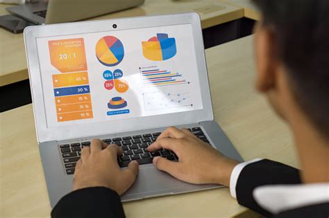 정장을 입은 사업가의 뒷모습은 사무실의 책상에 앉아 노트북 컴퓨터 키보드로 타이핑하고 그래프와 여러 가지 색상의 차트로 프리젠 테이션을합니다 20 24세에 대한 스톡 사진