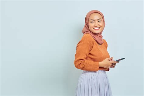 갈색 스웨터와 흰색 배경에 고립 된 휴대 전화를 사용하여 히잡에있는 쾌활한 젊은 아시아 무슬림 여성의 초상화 무슬림 생활 방식 개념 25 29세에 대한 스톡 사진 및 기타