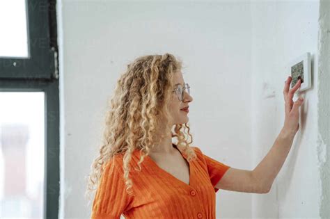 Woman Adjusting Temperature On Thermostat At Home Stock Photo