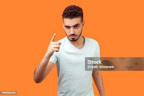 조심하세요 제기 손가락 제스처와 함께 당신을 경고 하는 엄격한 보스 갈색 머리 남자의 초상화입니다 오렌지 배경에 고립 된 실내 스튜디오 샷 20 29세에 대한 스톡 사진 및