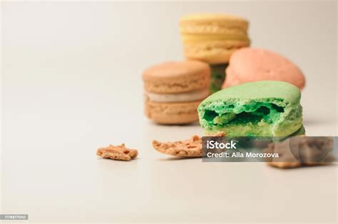 전경에 있는 녹색 마카롱 한 개에 물린 다 인근에는 프랑스 제과에서 나온 부스러기가 있습니다 배경에는 세 개의 신선한 색깔의 마카롱이 더미에 놓여 있습니다 고립 된 배경에