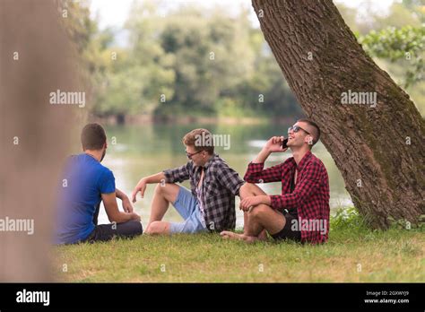 Group Of Young Men Enjoying The Nature Sitting On The Bank Of The River