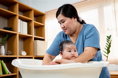 싱글맘은 물을 사용하여 비누를 몸에서 씻어 내고 유아 딸의 얼굴은 하루가 끝날 때 샤워를 한 후 더운 날씨로 인해 낮에 소녀를 목욕 시켰습니다 2 5 개월에 대한 스톡 사진