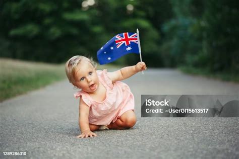 귀여운 사랑스러운 백인 아기 소녀는 호주 국기를 흔들어 호주의 날 휴가를 축하하는 공원에서 길가에서 기어 다니는 재미있는 아이 1 월 야외에서 국가 호주의 날 축하 1월에