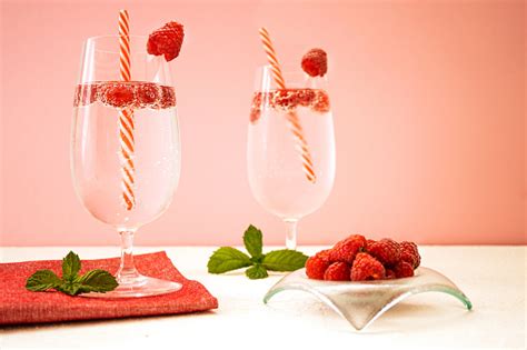 안경에 라스베리를 곁들인 상쾌한 여름 음료는 분홍색 벽에 흰색 테이블 위에 서 있습니다 근처에는 잘 익은 향기로운 나무 딸기 한 그릇이 있습니다 안경은 딸기와 칵테일 튜브로