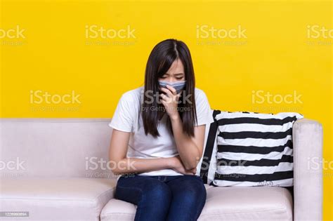 소파에 앉아 있는 아시아 여성 기침이나 재채기를 하는 보호용 얼굴 마스크를 착용하고 있다 독감에 걸린 아픈 여성은 마스크를 쓰고 아프고 기침을 하고 독감에 대한 마스크를