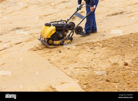 Worker Using Vibratory Plate Compactor For Compaction Sand During Path Construction Stock Photo