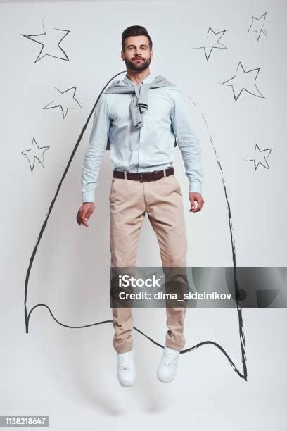 슈퍼 히어로 자신감 수염 남자의 전체 길이 그려진 된 케이프를 입고 그것에 별의 그림과 회색 배경에 대해 스튜디오에서 뛰어