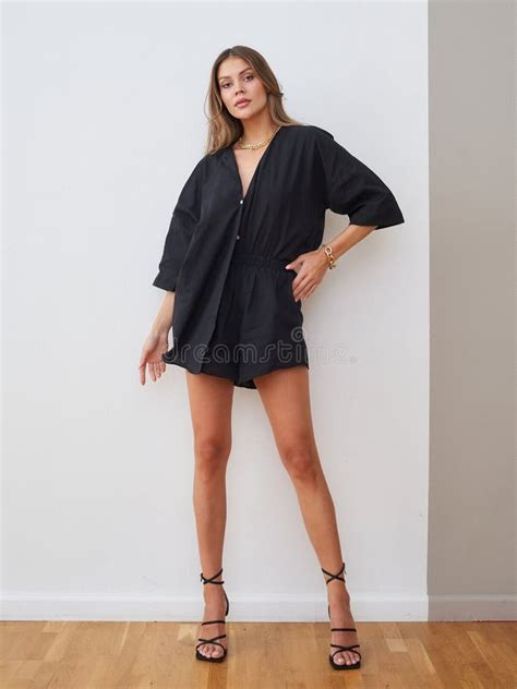 Woman In An Elegant Black Romper And High Heels Stands Confidently With