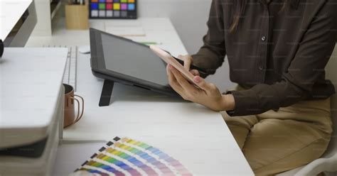 웃고 있는 여성 그래픽 디자이너가 직장에 앉아 휴대폰을 사용하여 친구들과 문자 메시지를 보내거나 마사지하는 장면을 자릅니다